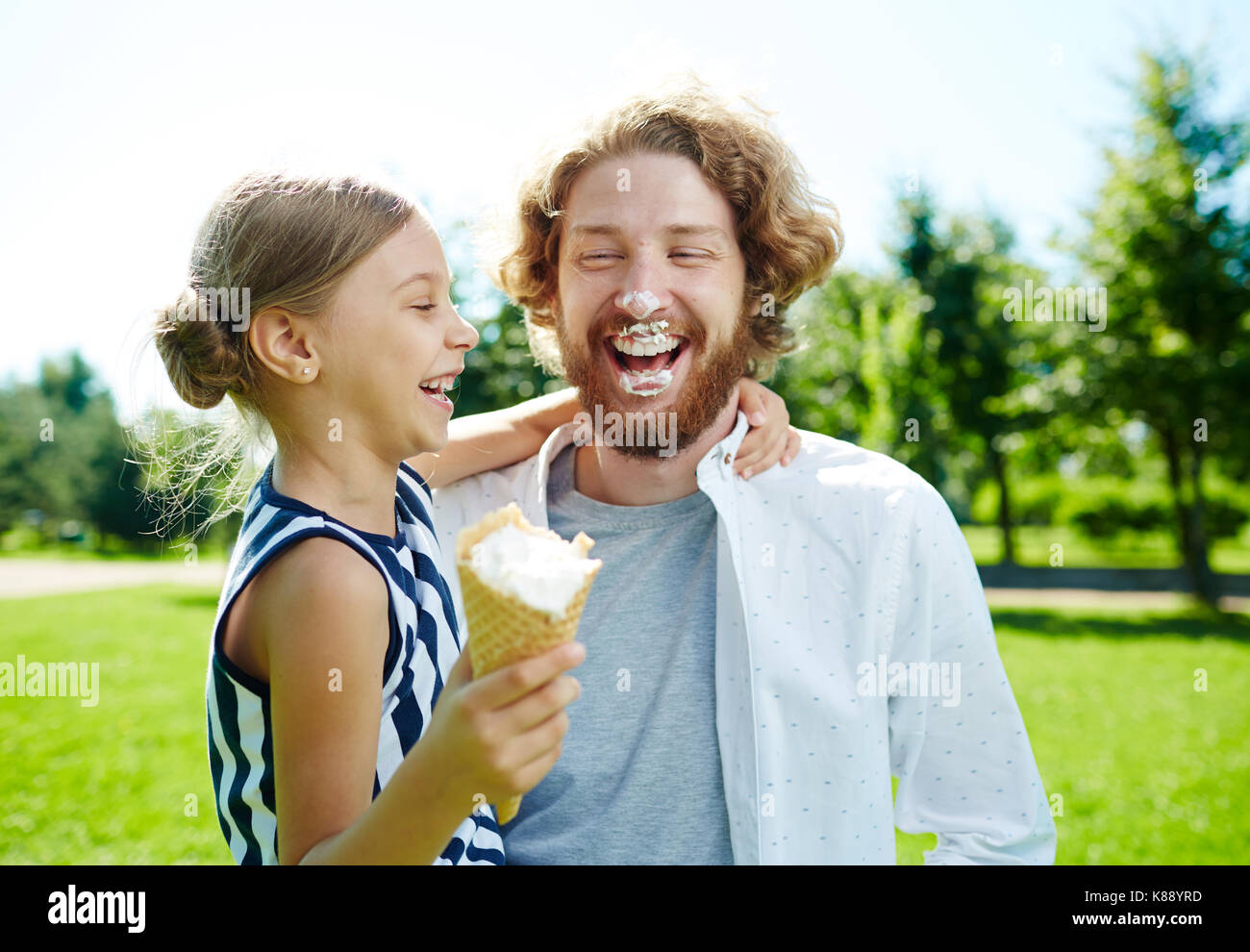 Laughing girl with ice-cream and her father having fun in park at ...