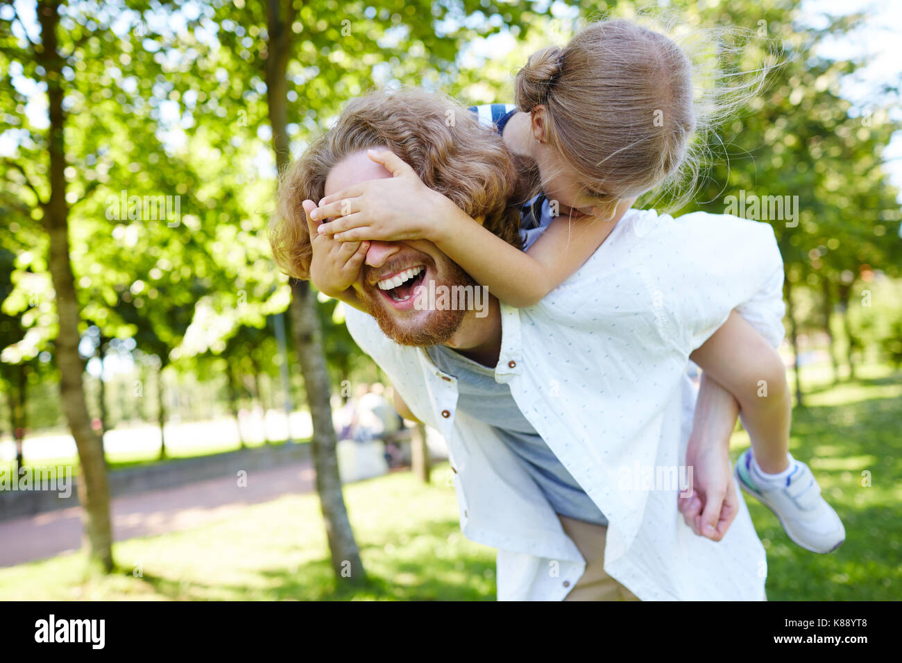 Laughing man holding his daughter on back during play in park Stock ...