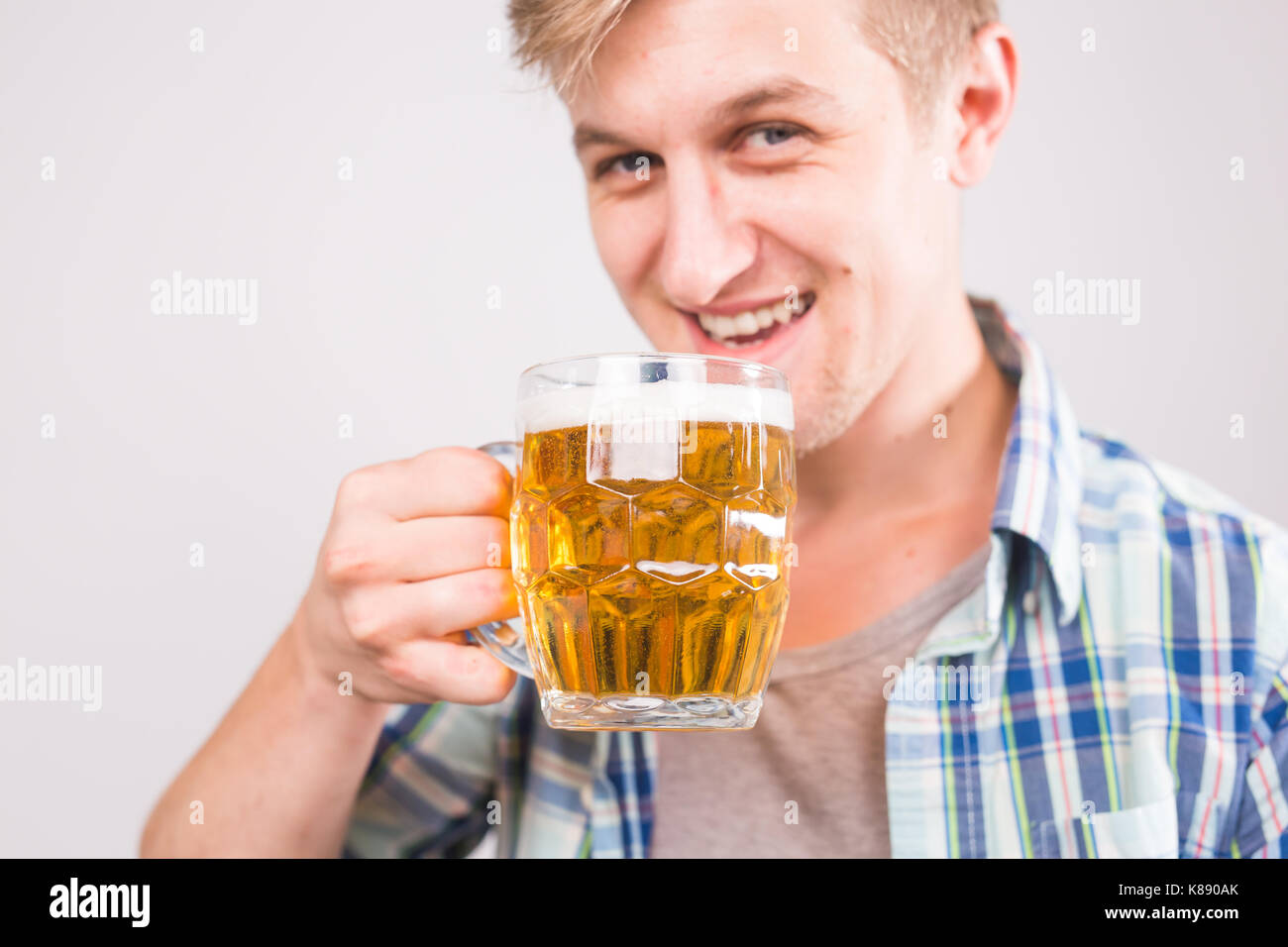 Cheerful young man holding a beer mug full of beer and smiling on white ...
