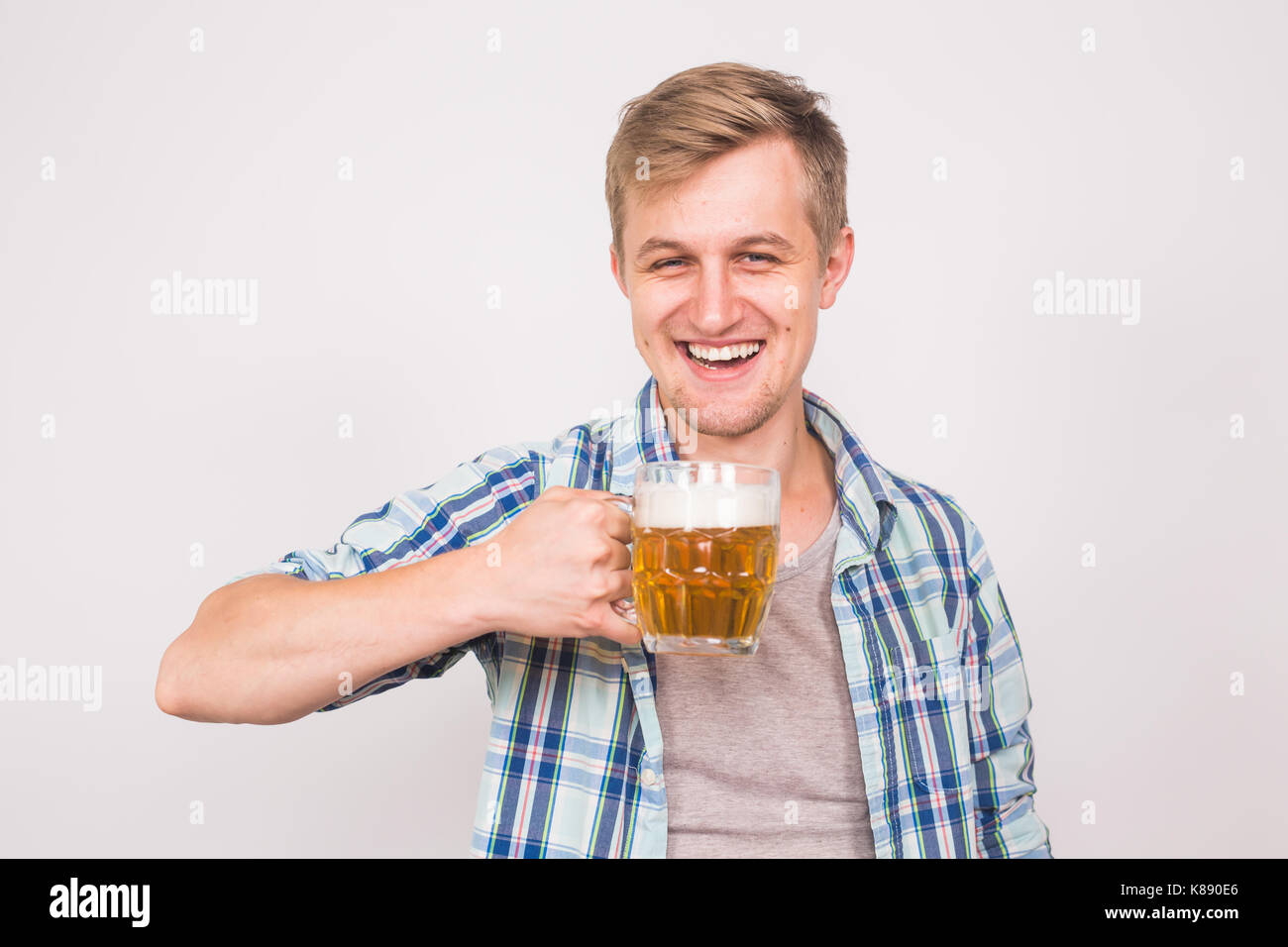 Cheerful young man holding a beer mug full of beer and smiling on white ...