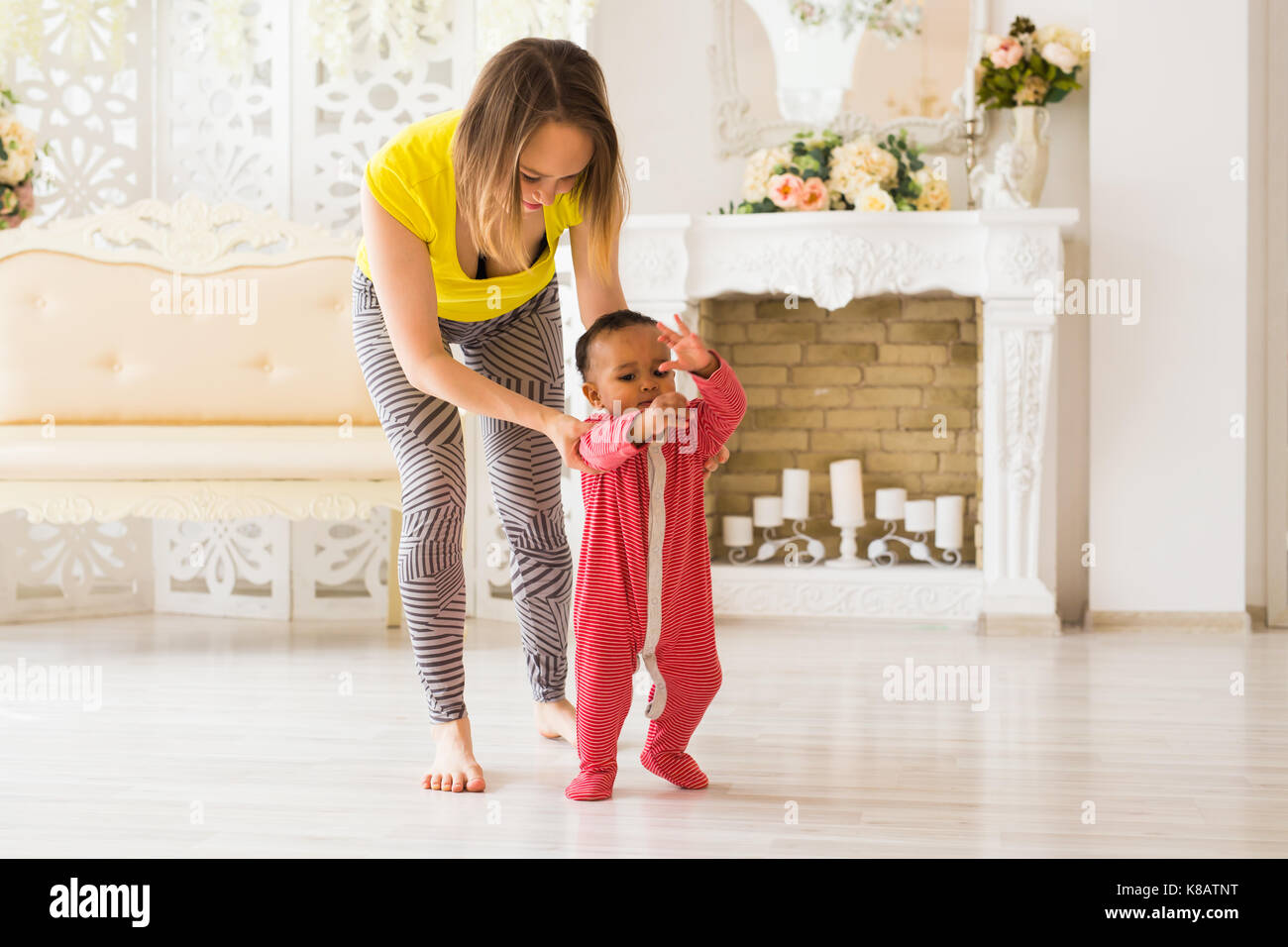 Cute little mixed race baby learning to walk, mom is holding his hands ...