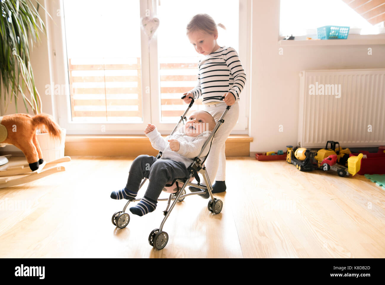 Little girl at home with baby brother in toy stroller Stock Photo - Alamy