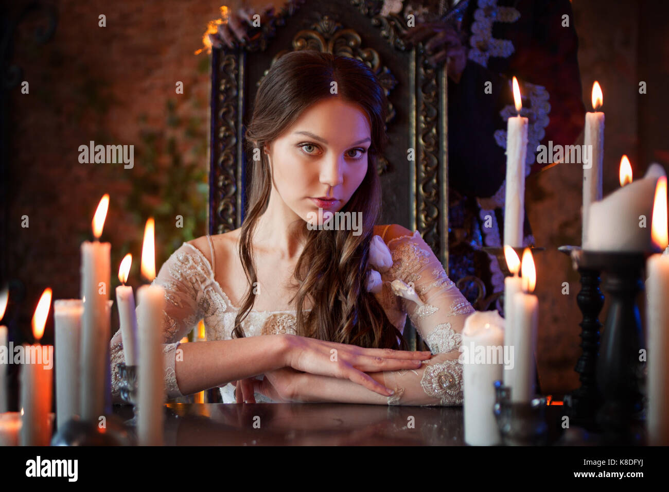 Beautiful young woman in vintage dress, at a table in the mystic manor ...