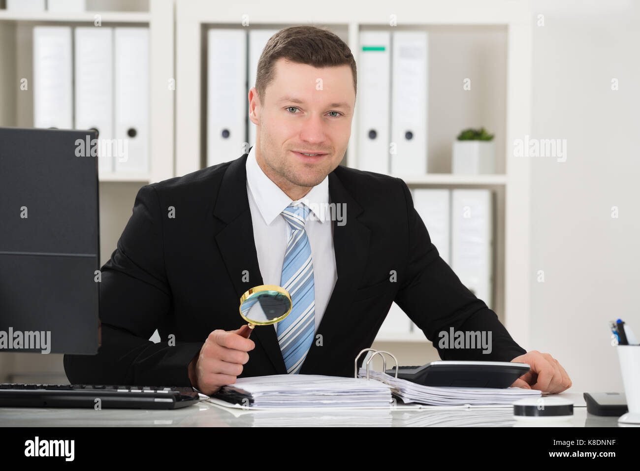 Male accountant analyzing invoice with magnifying glass at desk in ...