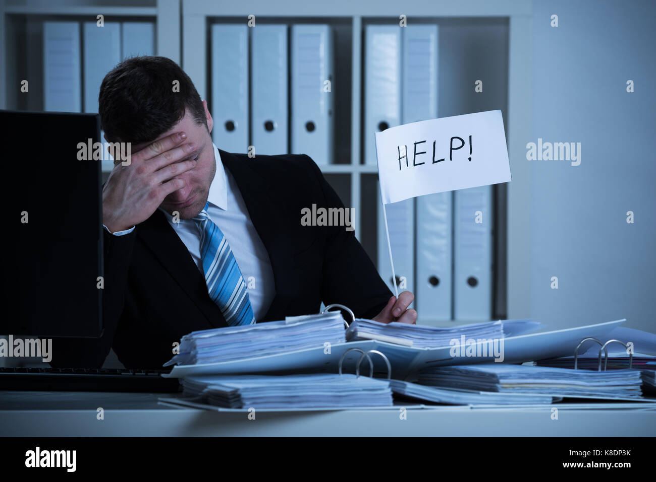 Stressed accountant holding help sign at desk while working late in ...