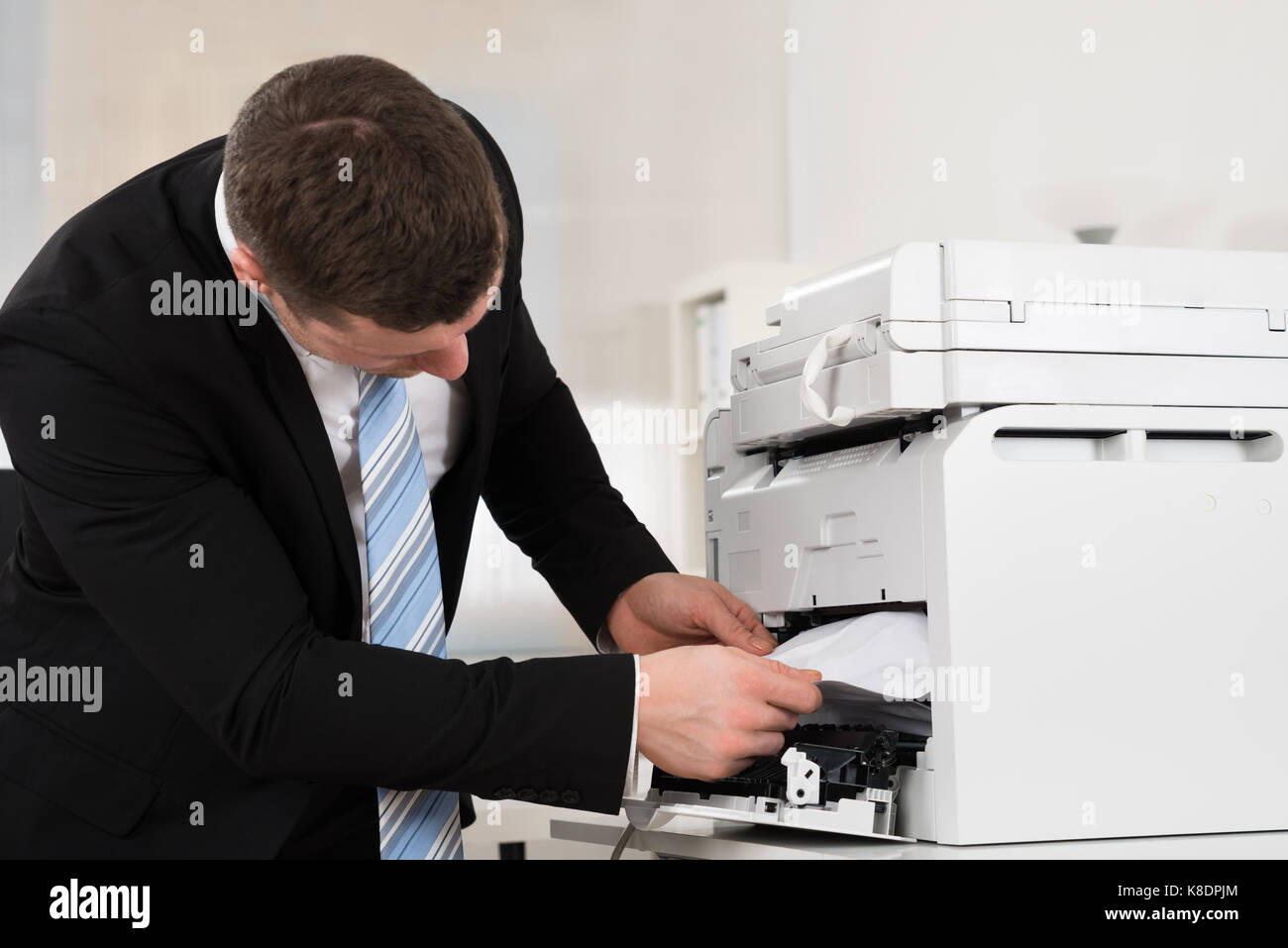Mid adult businessman removing paper stuck in printer at office Stock ...