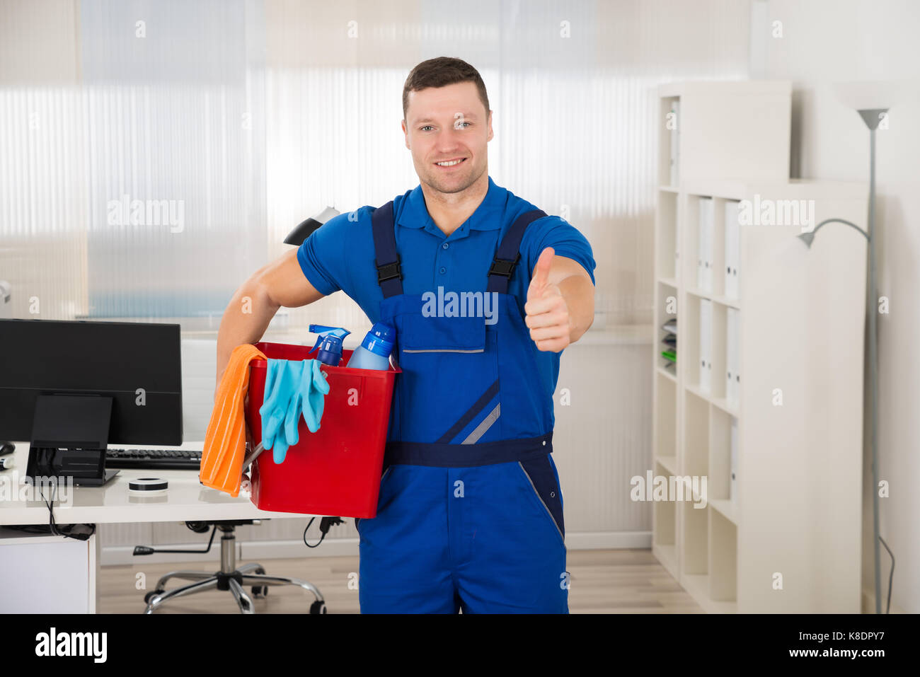 Portrait of happy male janitor showing thumbs up while carrying bucket ...