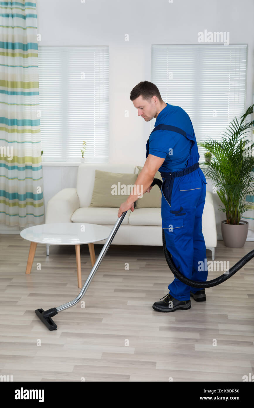 Full length side view of worker cleaning floor with vacuum cleaner at ...
