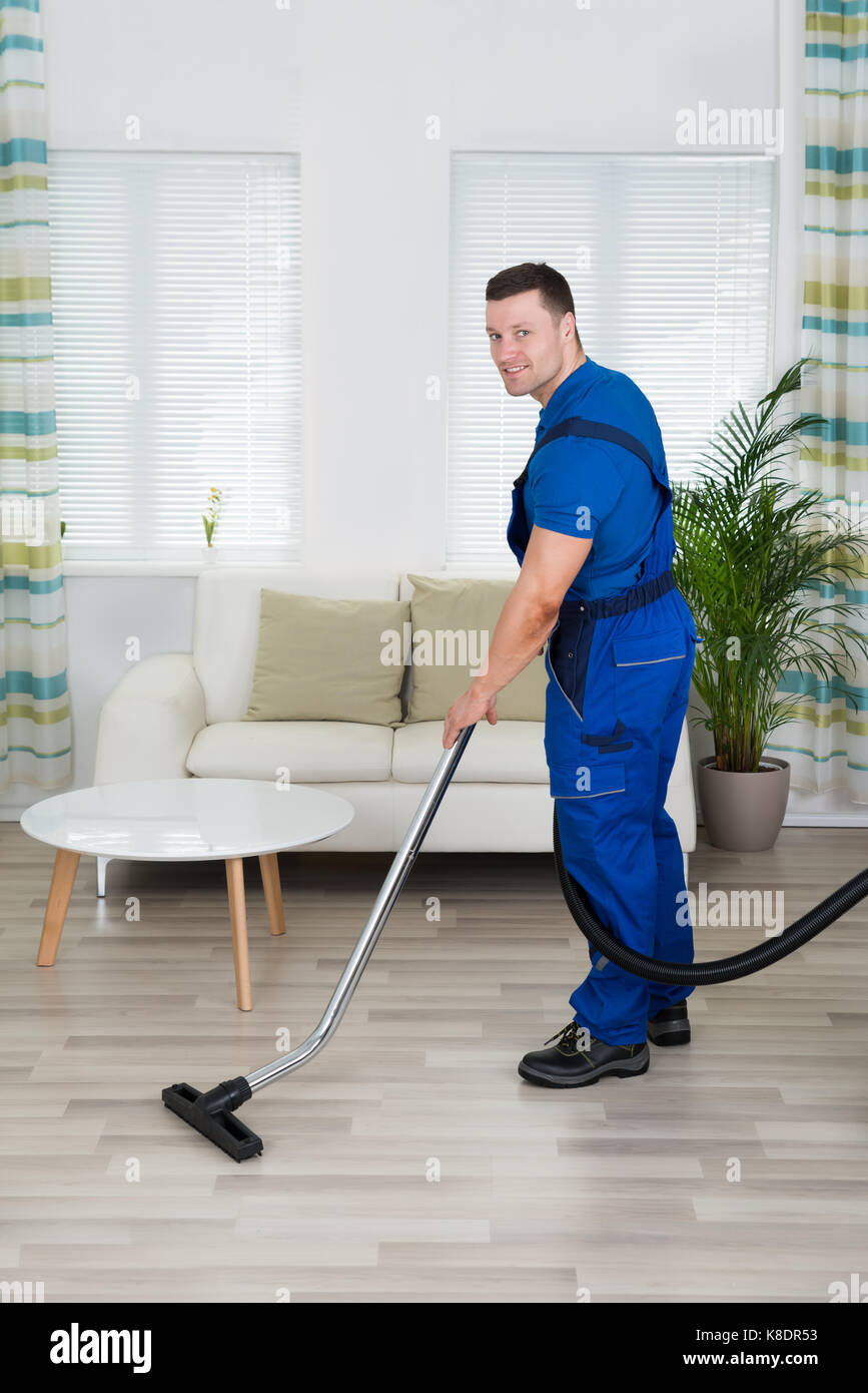 Full length side view of worker cleaning floor with vacuum cleaner at ...