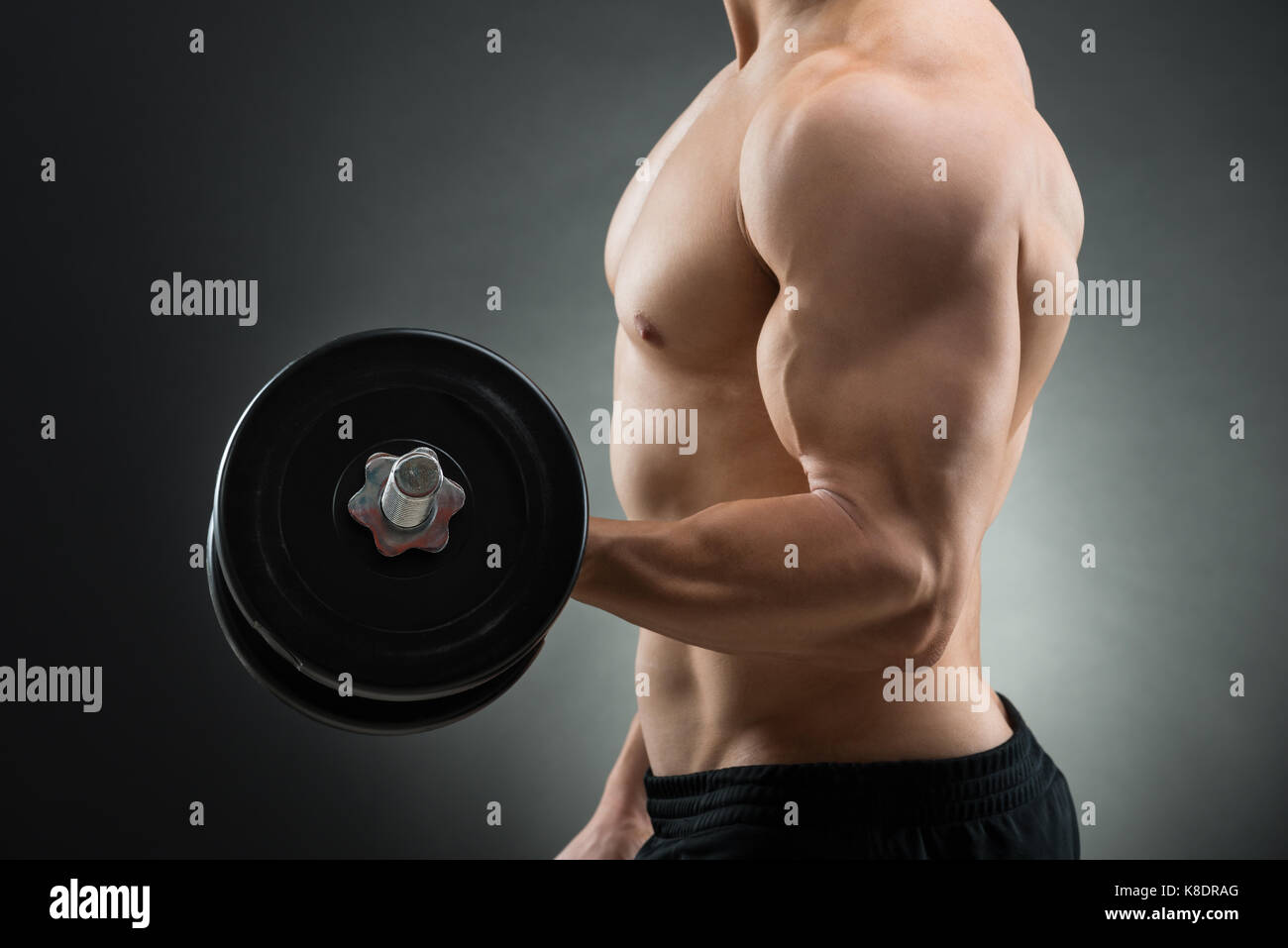 Midsection side view of muscular man lifting dumbbell against black ...