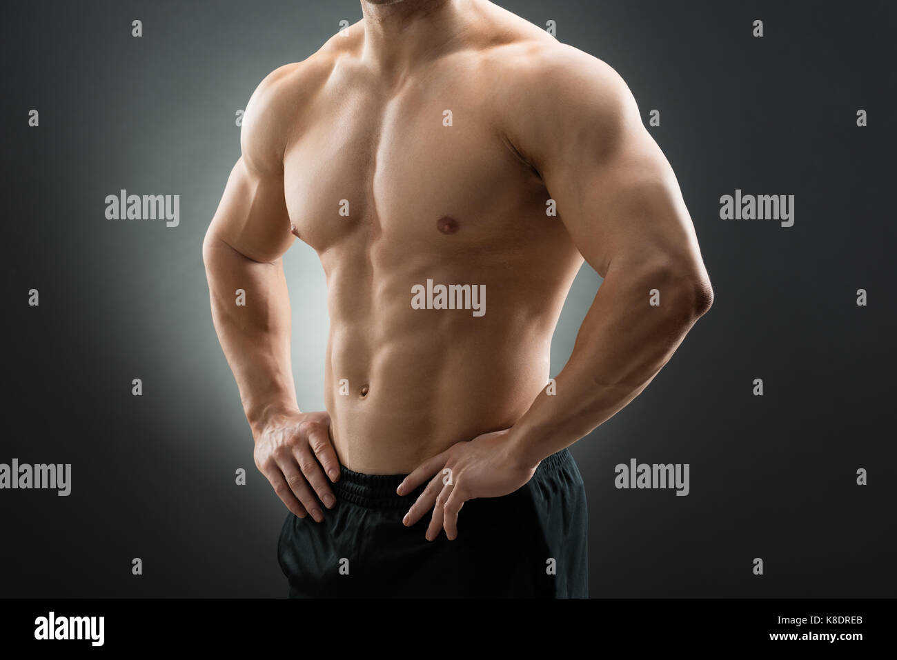 Midsection of muscular man standing with hands on hip against black ...