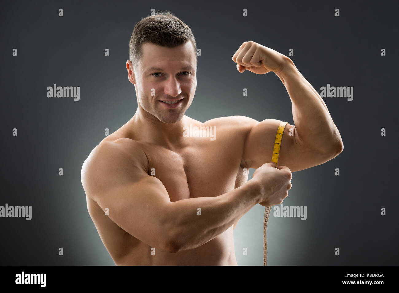 Portrait of happy muscular man measuring bicep with measure tape ...