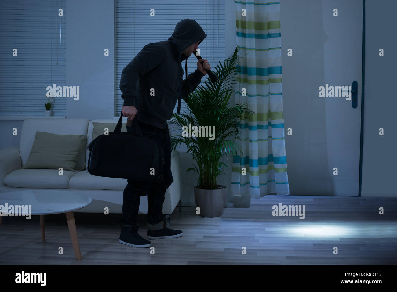 Full length of robber with flashlight and bag walking in living room ...
