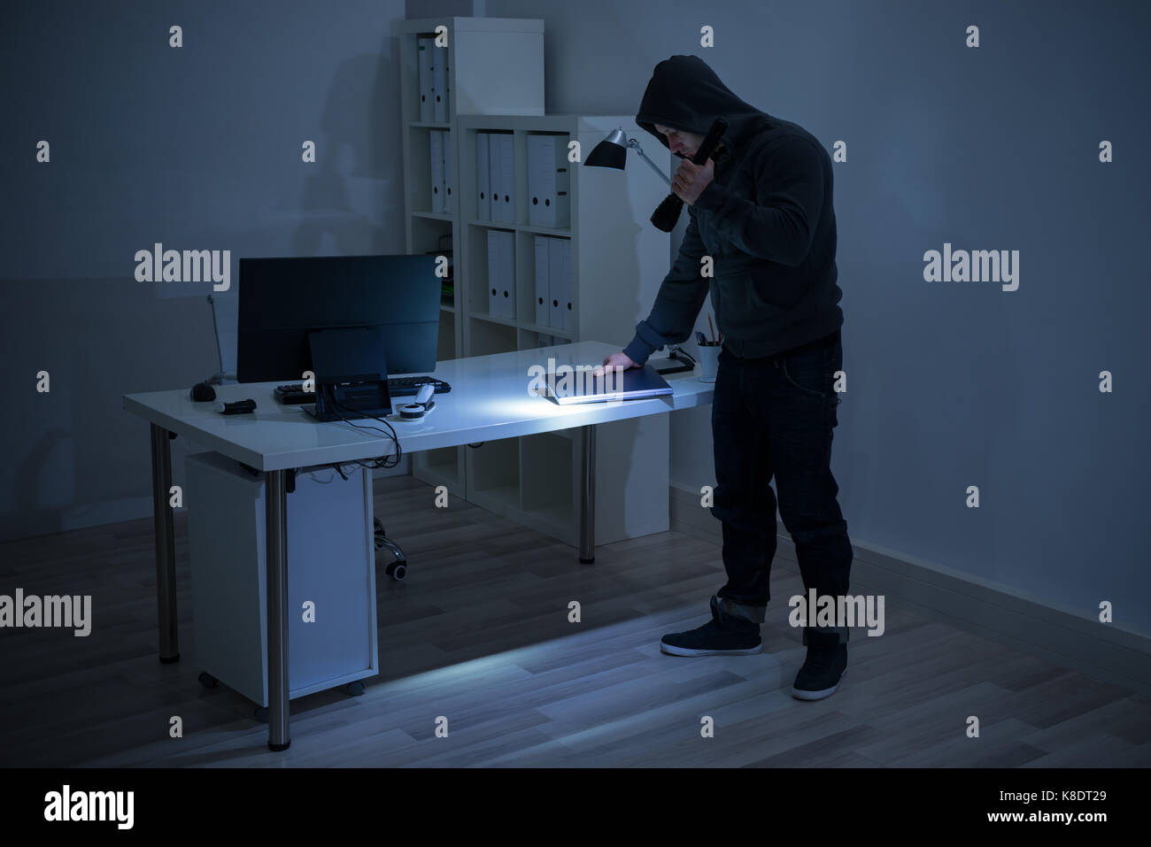 Full length of robber with flashlight holding laptop at desk in office ...