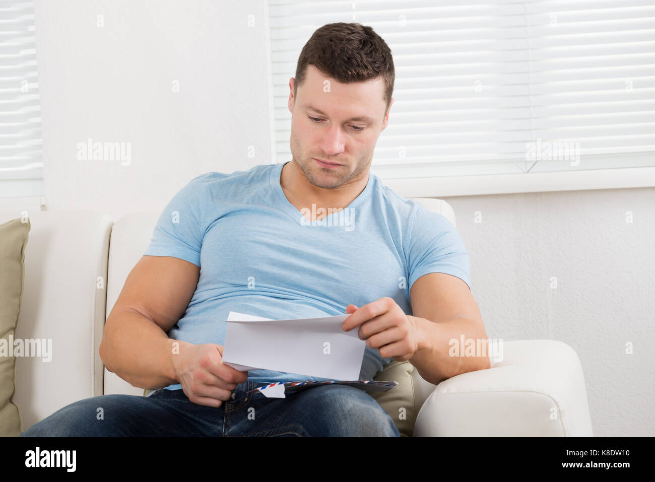 Serious mid adult man reading letter on couch at home Stock Photo - Alamy