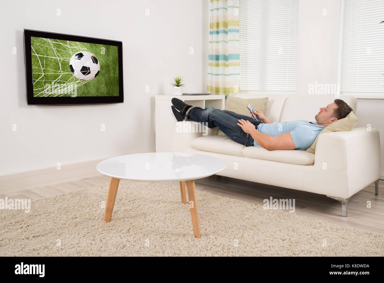Relaxed mid adult man lying on sofa while watching football match on ...