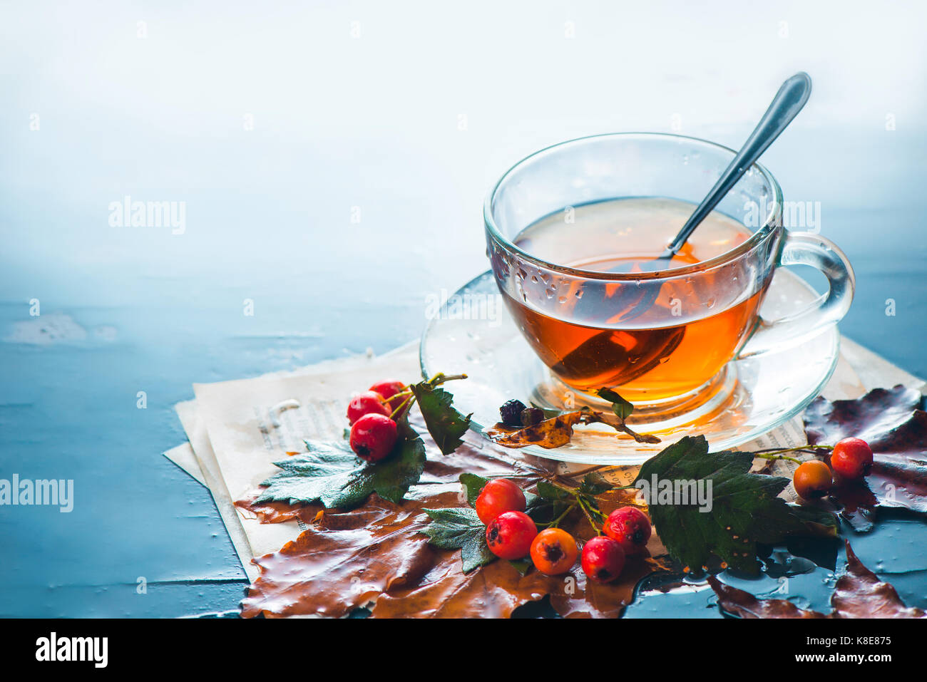 Glass tea cup in autumn still life with rain, leaves, book pages and ...