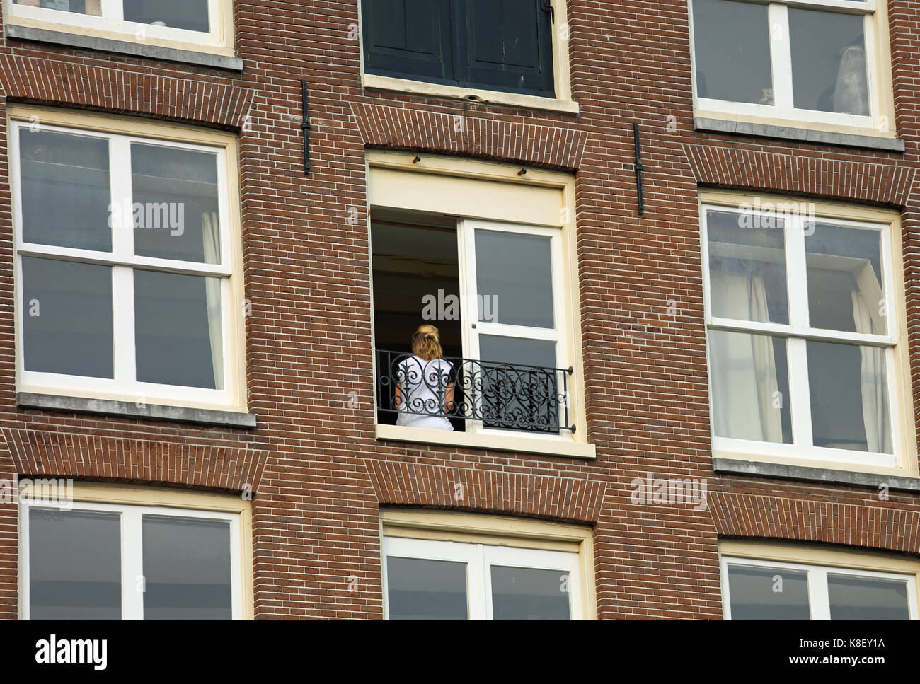 young blonde girl at the apartment building window in an european city ...