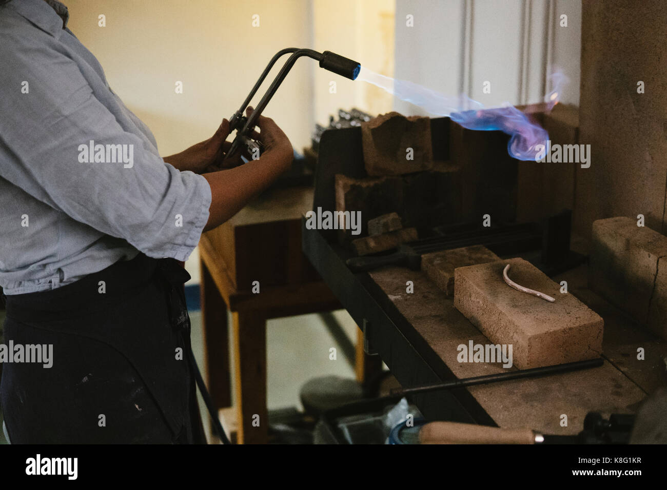 Mid section of female jeweller using flaming blow torch at workbench ...