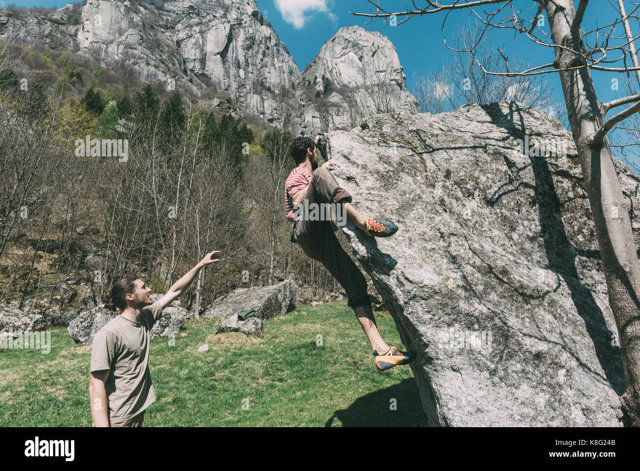Young male boulderer pointing for woman climbing boulder, Lombardy ...