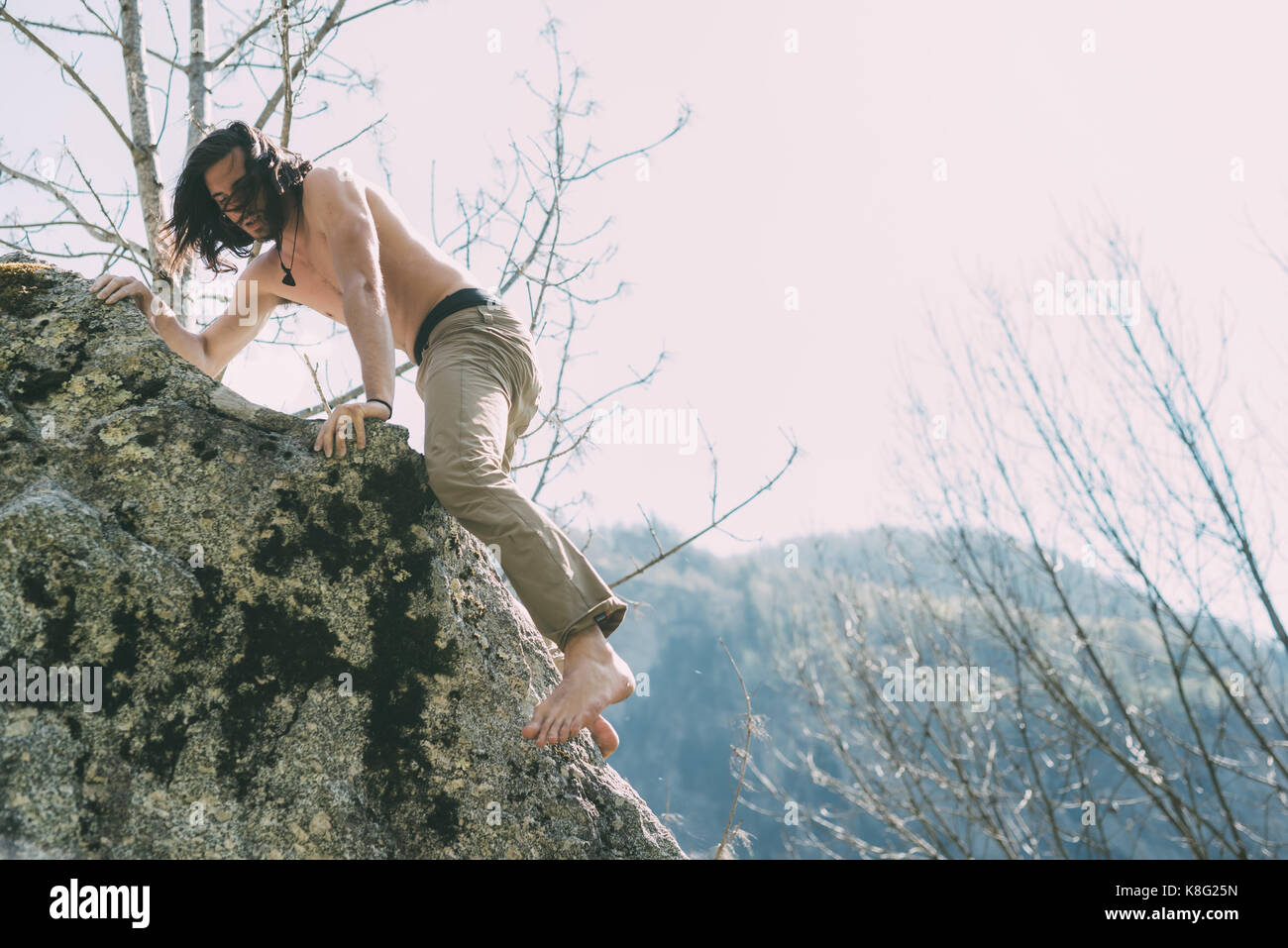 Bare chested and bare foot male boulderer climbing boulder, Lombardy ...