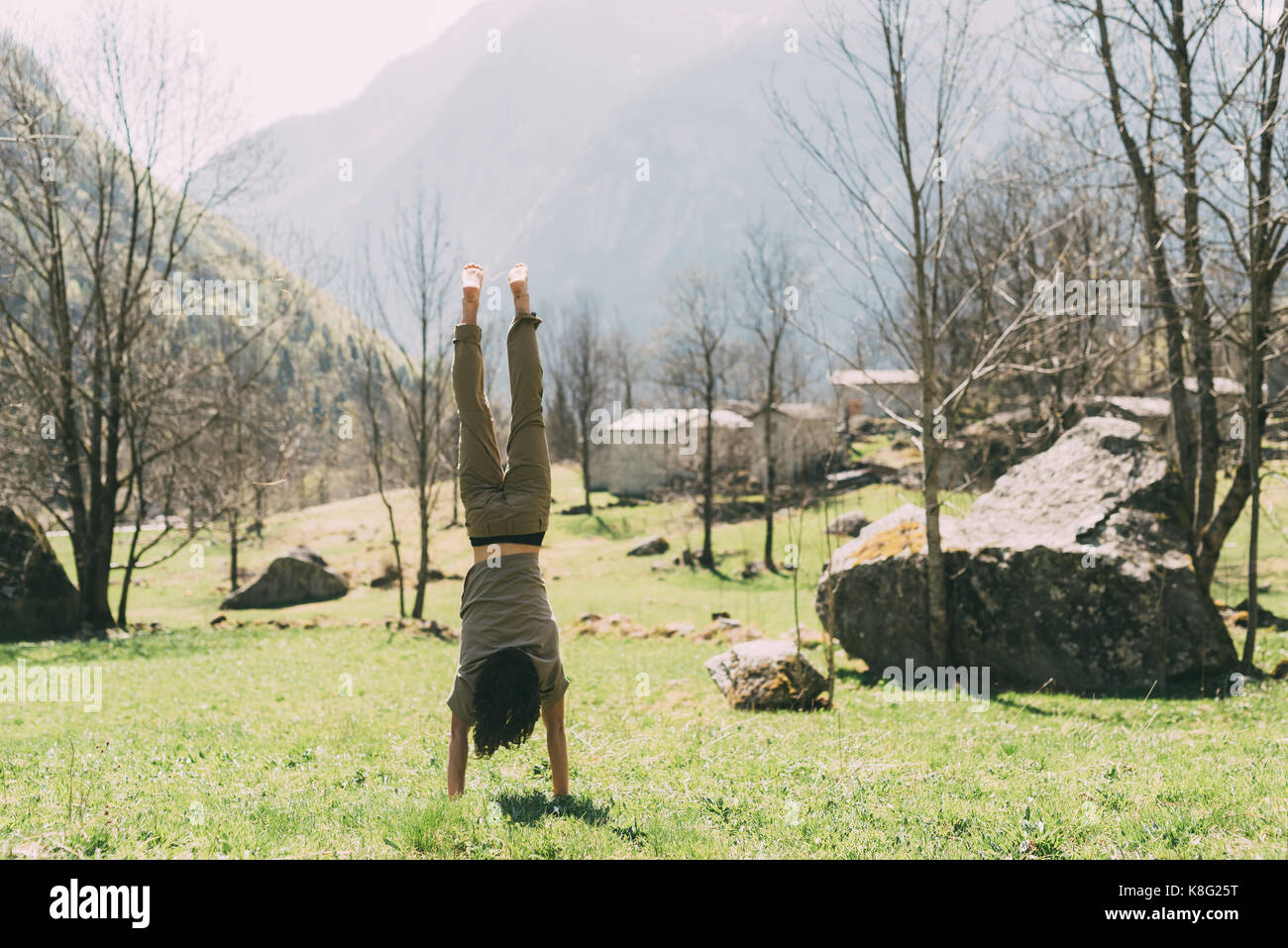 Rear view of young male boulderer doing handstand in valley, Lombardy ...