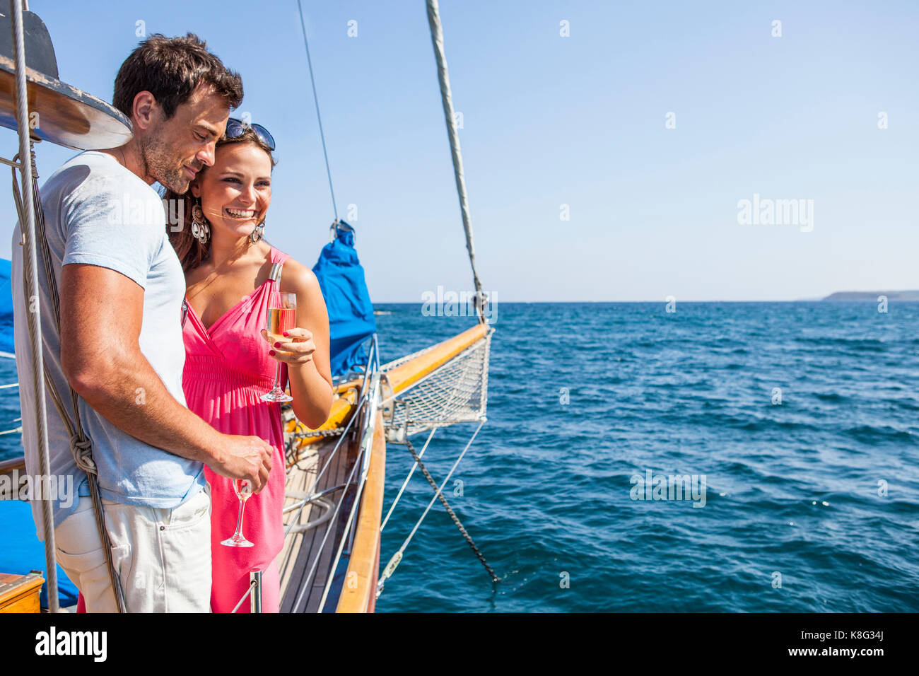 Couple standing on boat, on water, holding champagne flutes, looking at ...