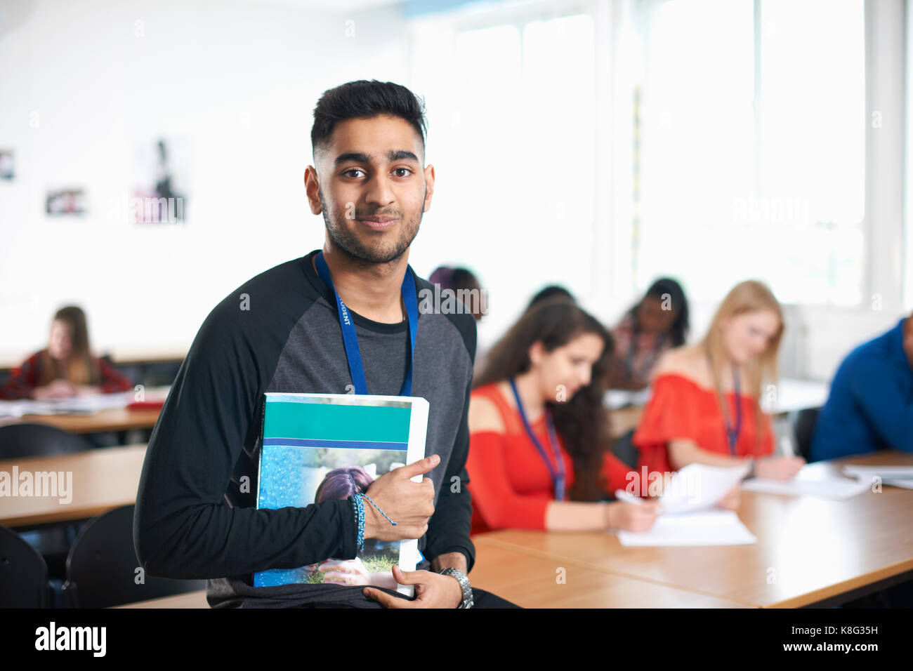 Portrait of student in classroom holding textbook looking at camera ...