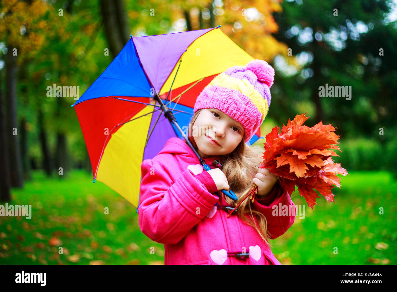 happy girl with a colorful umbrella and red autumn leaves in he autumn ...