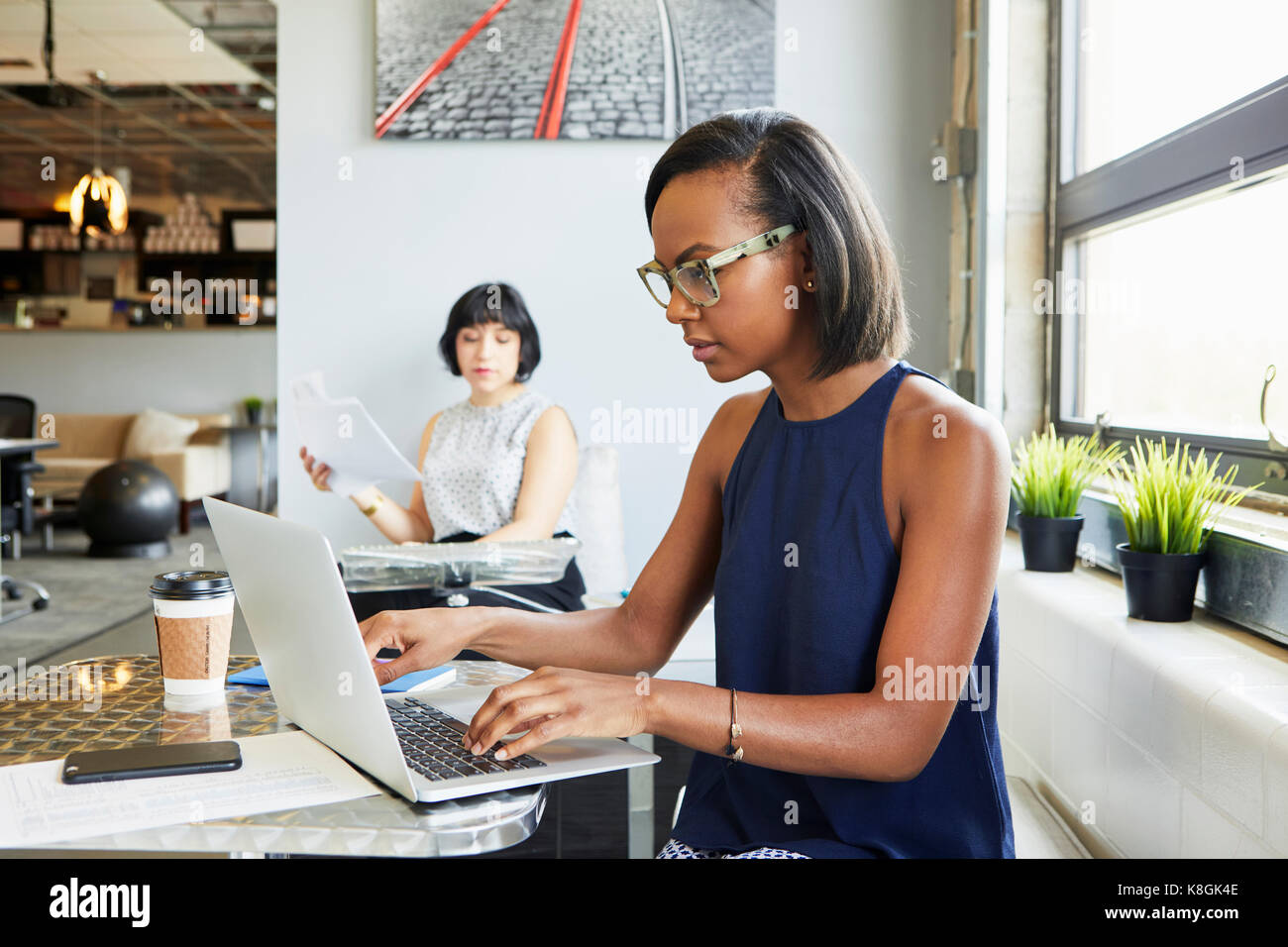 Woman sitting at desk, working on laptop in modern office Stock Photo ...