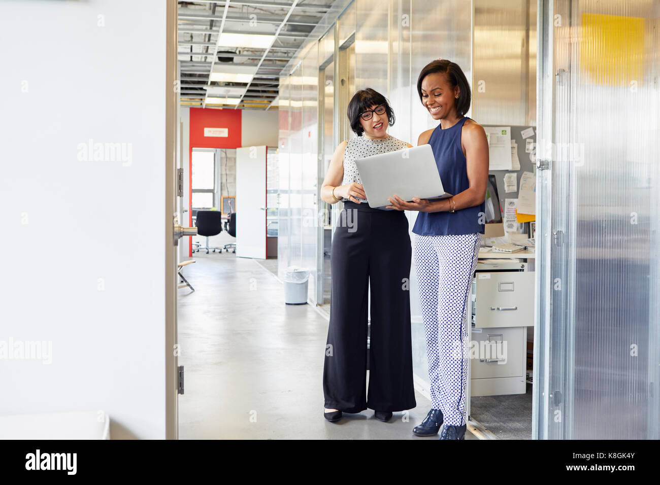 Two women standing in office corridor looking at laptop screen Stock ...