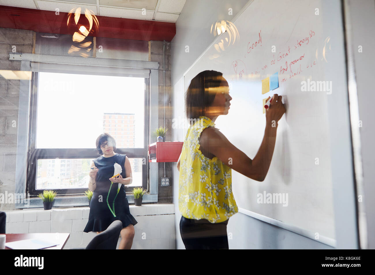 Two women in office, solving problem, using whiteboard, sticky notes ...