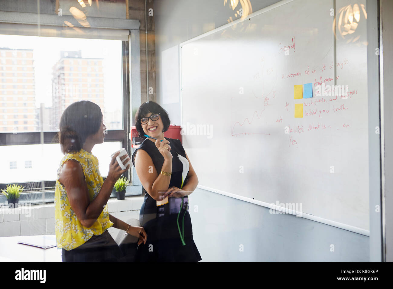 Two women in office, solving problem, using whiteboard, sticky notes ...