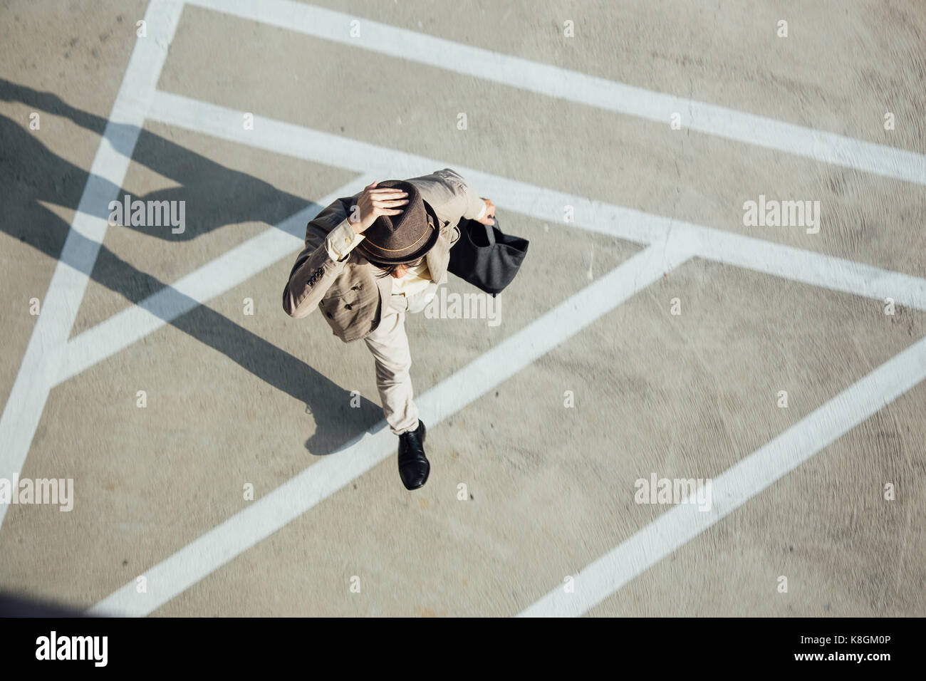 Young man walking across road, holding hat on head, overhead view Stock ...