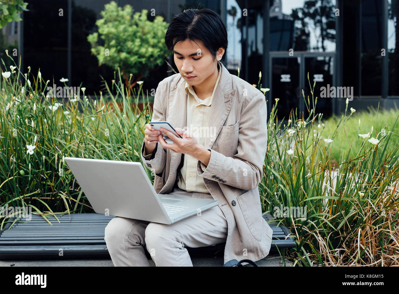 Young man sitting outdoors, using laptop, holding smartphone Stock ...