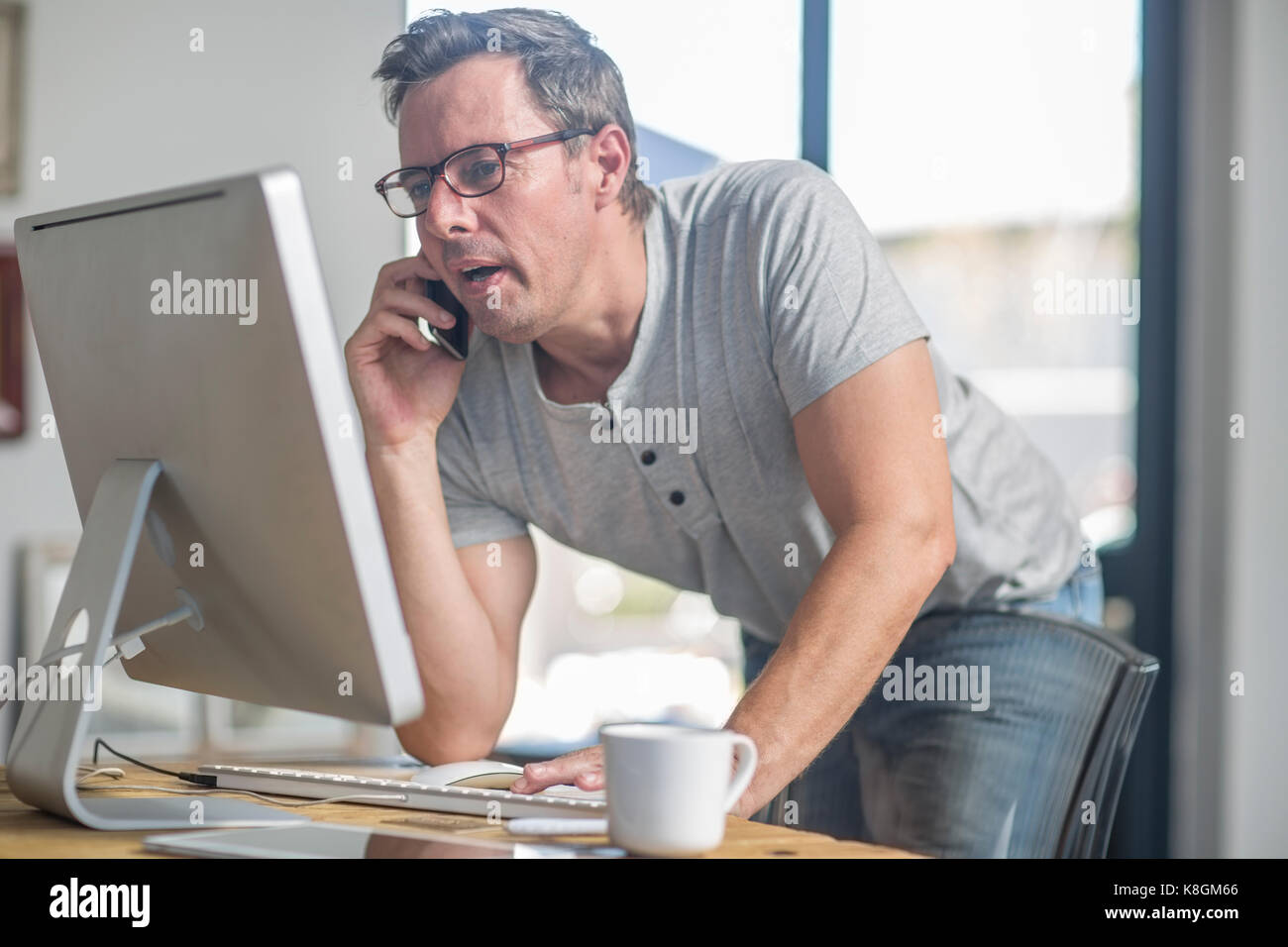 Man at computer using smartphone to make telephone call Stock Photo - Alamy