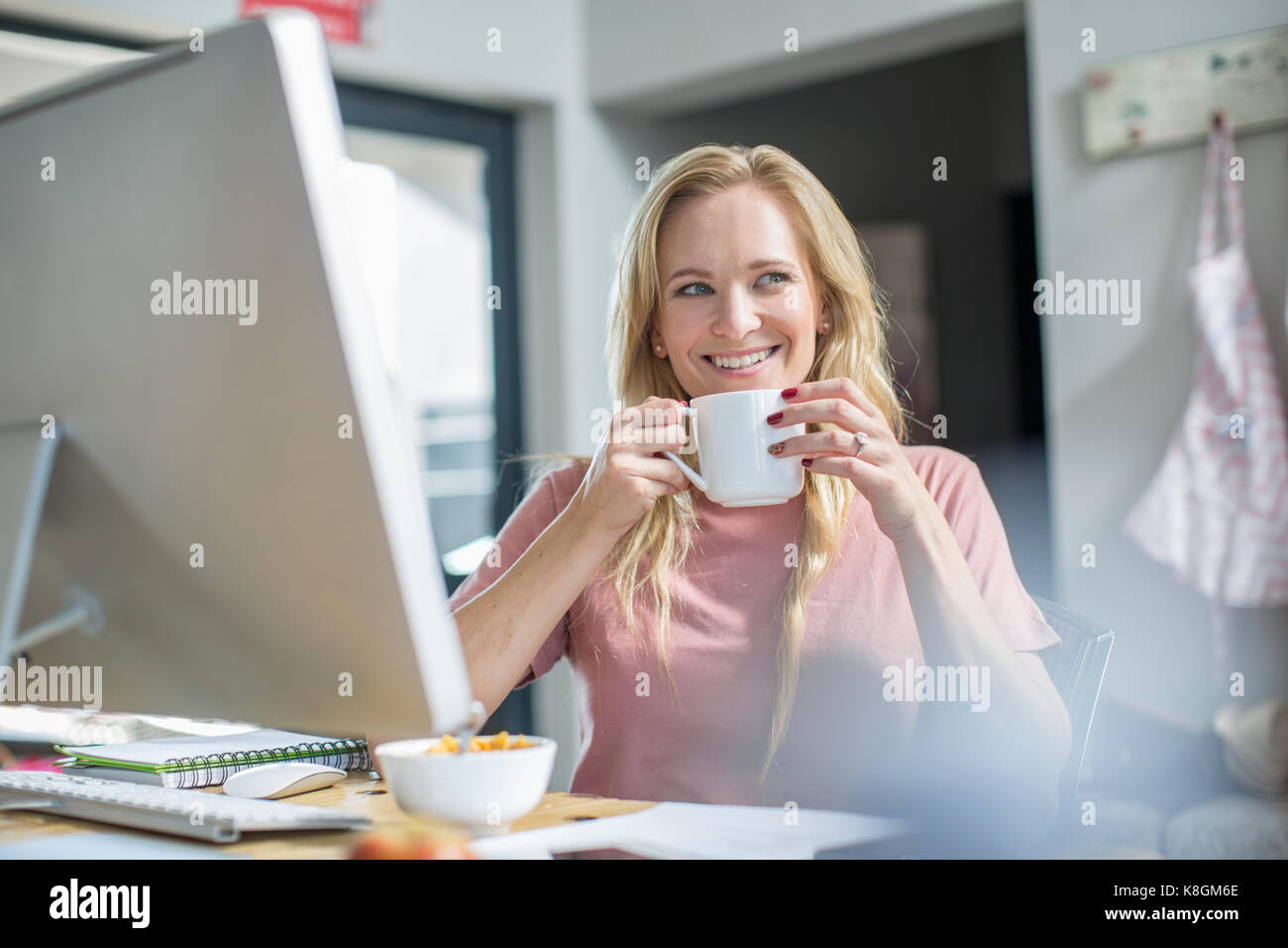 Woman at computer drinking coffee smiling Stock Photo - Alamy