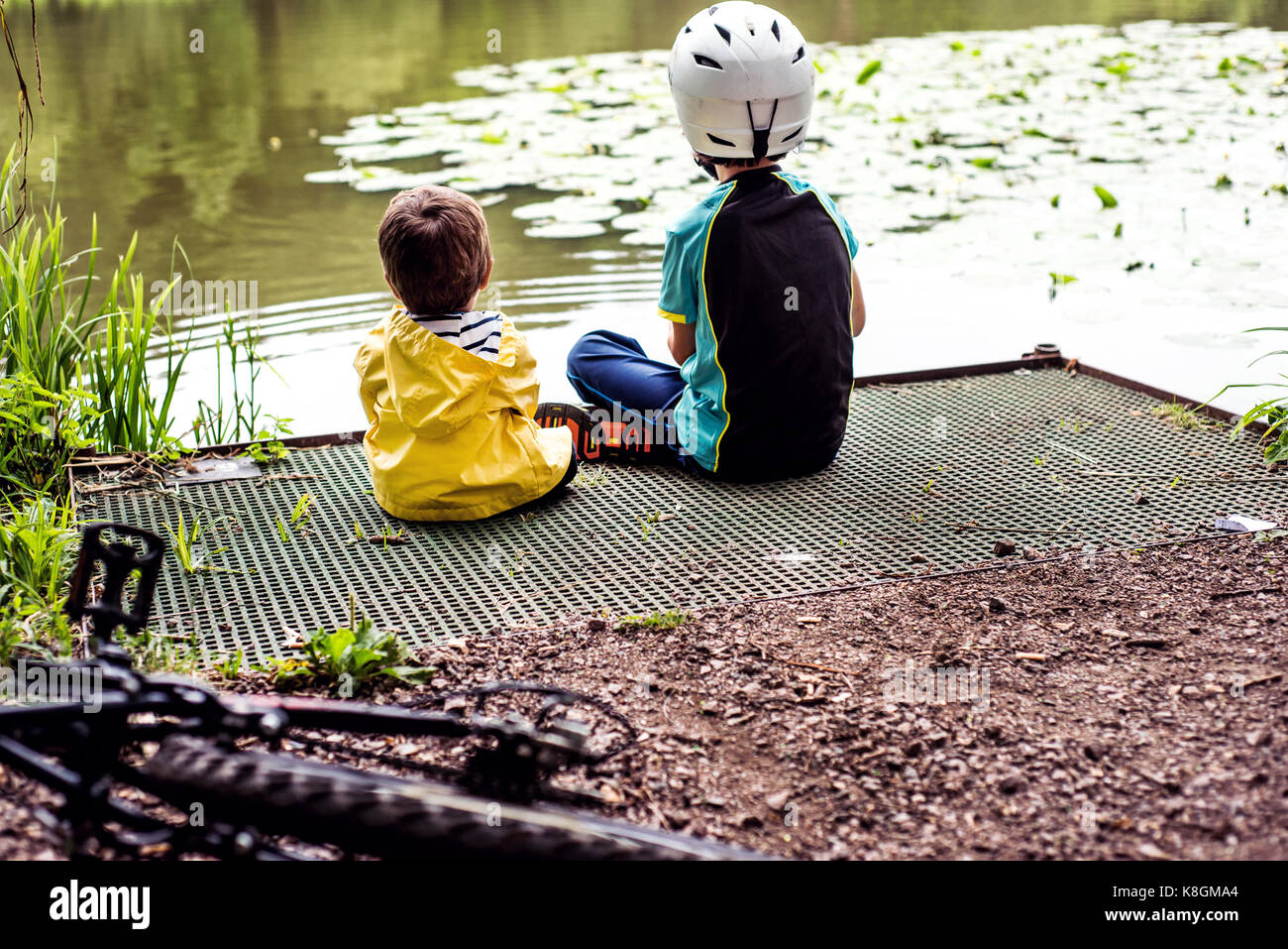 Two young brothers sitting at water's edge, rear view Stock Photo - Alamy