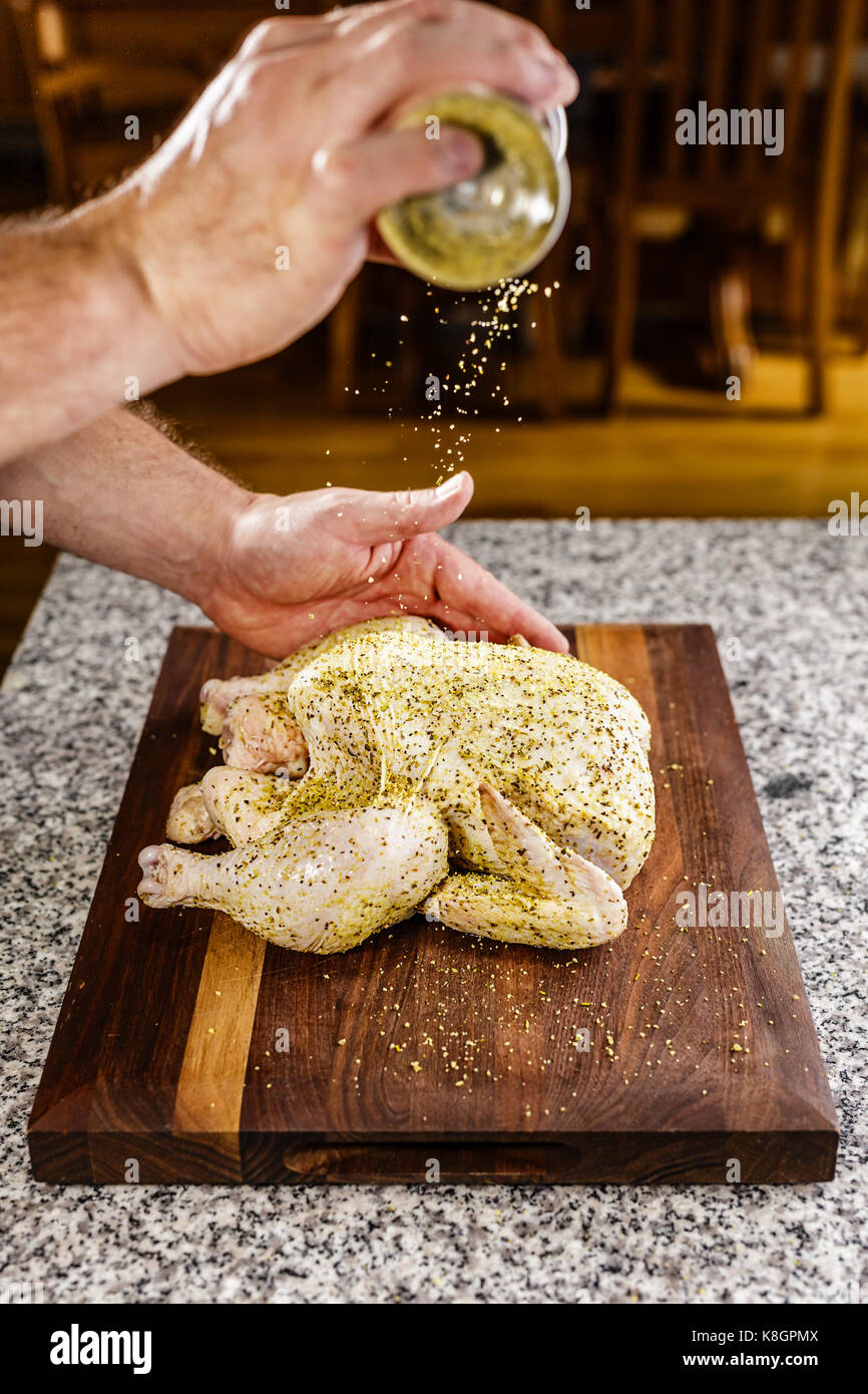 A whole chicken on a cutting board being seasoned with spices. A home ...