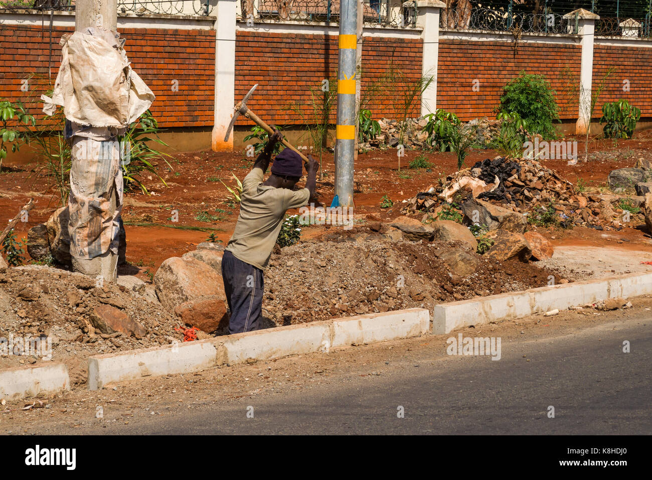 Construction worker digging hole with pickaxe by road, Nairobi, Kenya ...