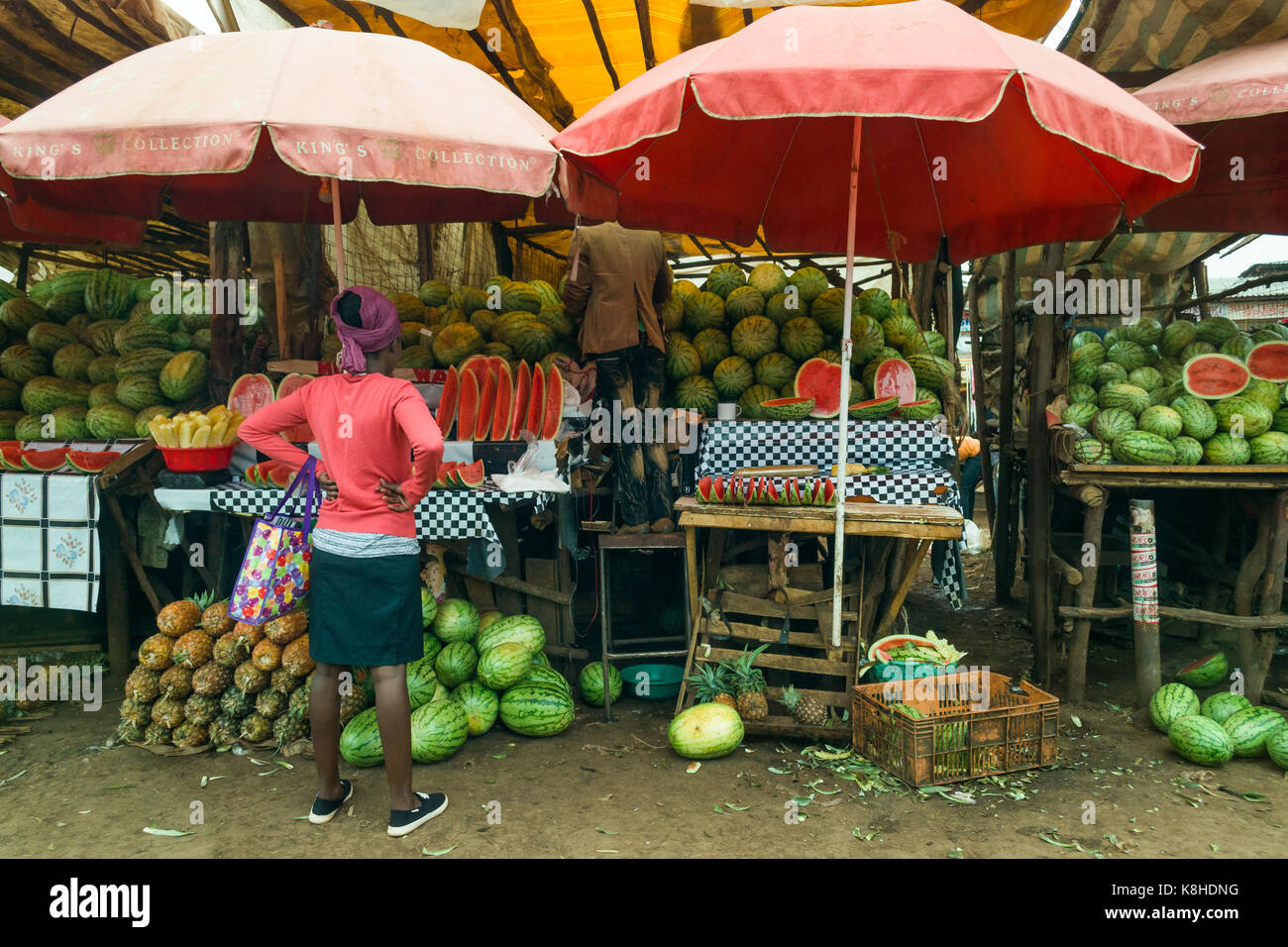 Woman stands waiting at watermelon stall as owner stands on stool in ...