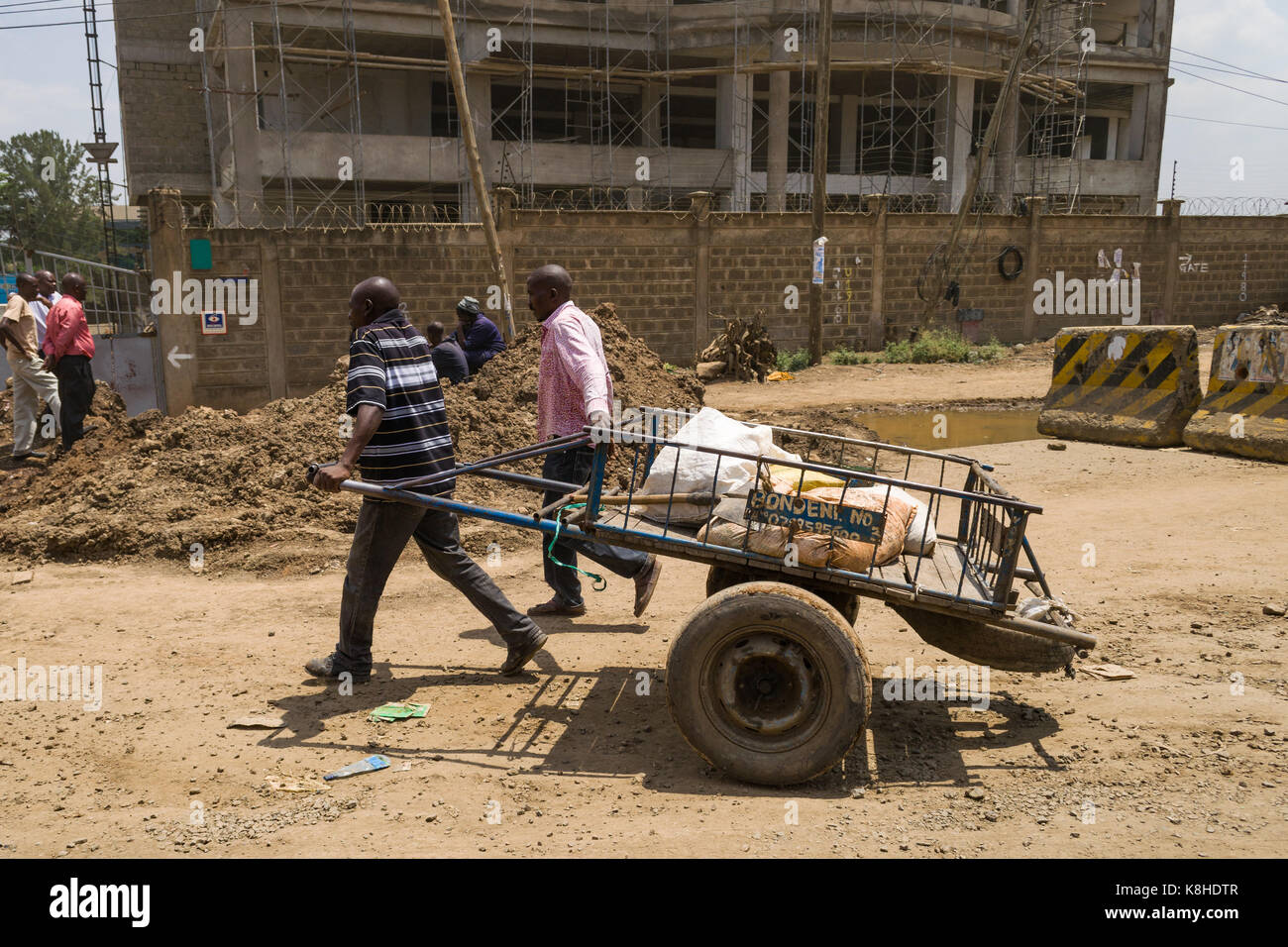 Two men pull a handcart with goods on along road with people and ...