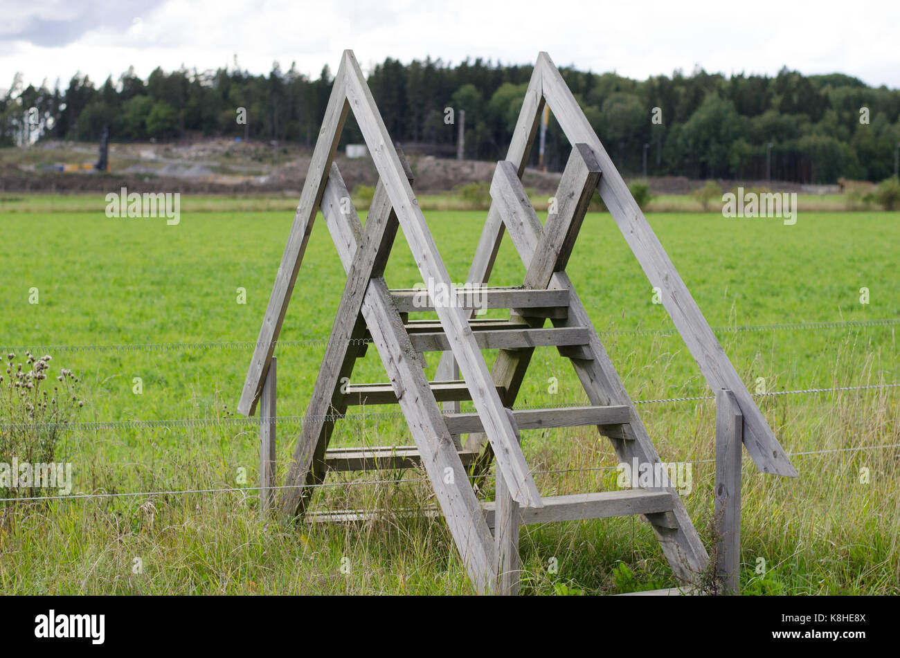 A stile over a fence on a meadow with construction in the background ...