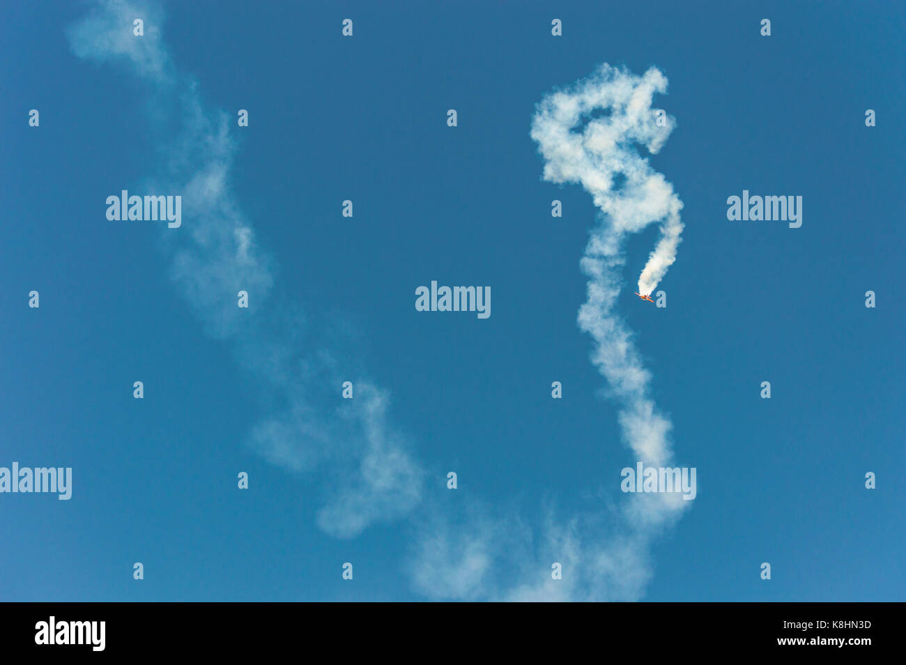 Aerobatic plane leaving a white smoke trail in the bright blue sky ...