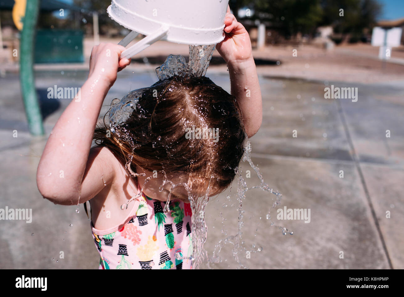 Girl emptying bucket of water on head at park Stock Photo - Alamy