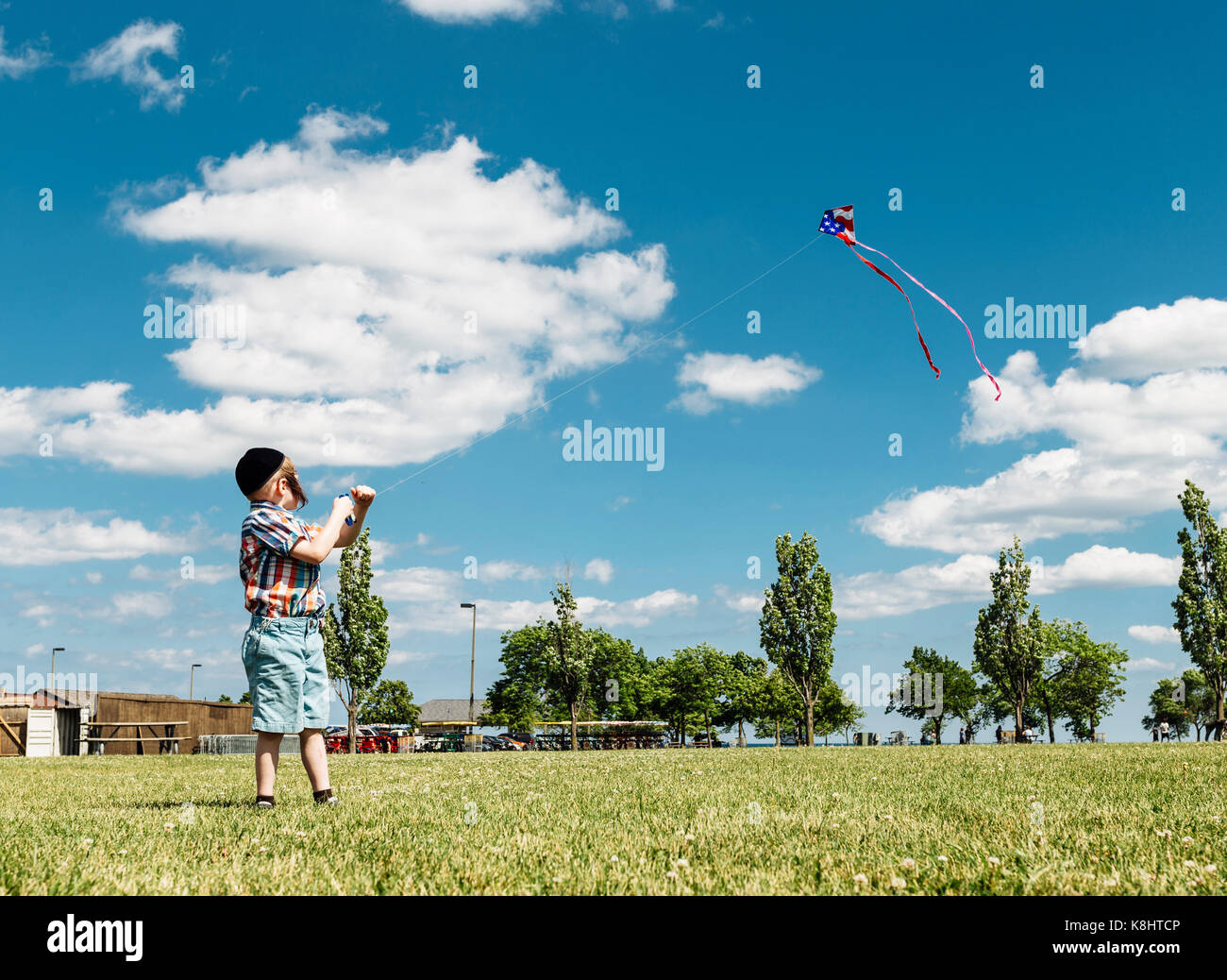 Full length of boy flying American Flag kite at park against cloudy sky ...