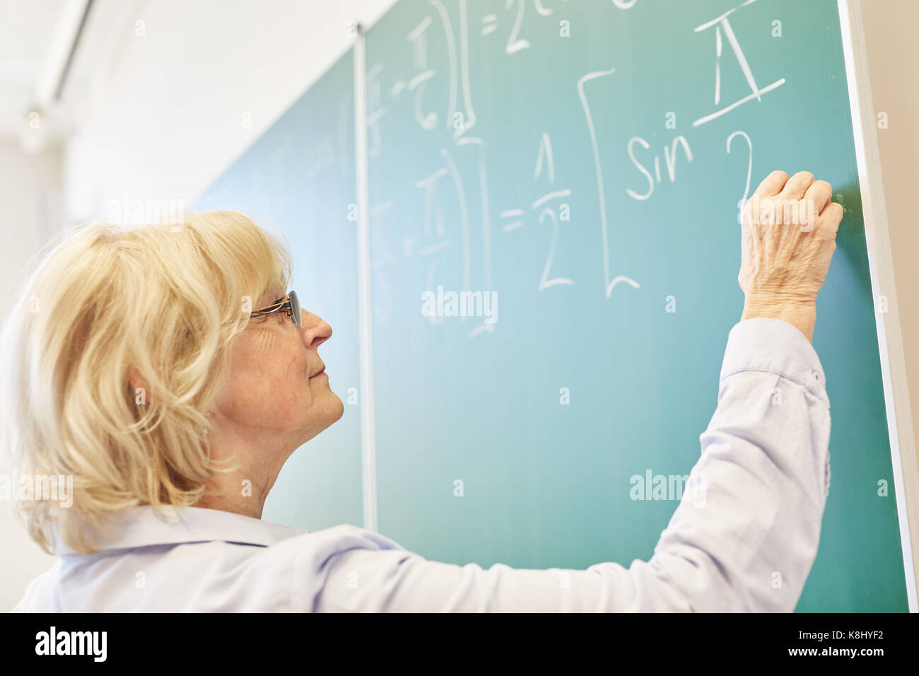 Senior woman as math university teacher writes on chalkboard Stock ...