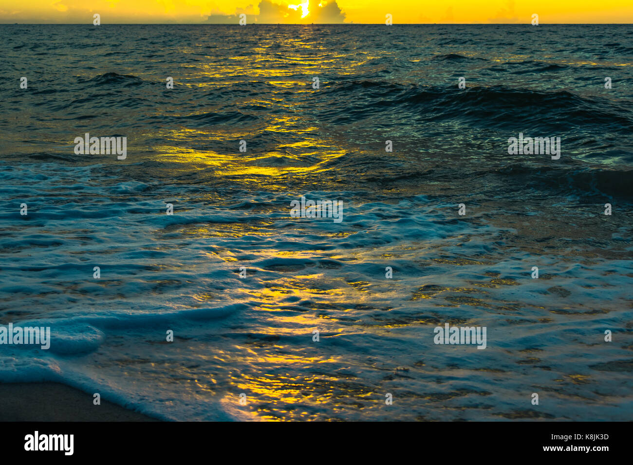 blue waves reflecting yellow sunshine on summer morning at the beach ...