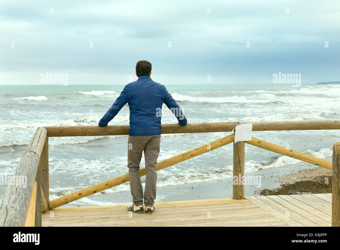 lonely men with blue jacket looking at the mess sea Stock Photo - Alamy