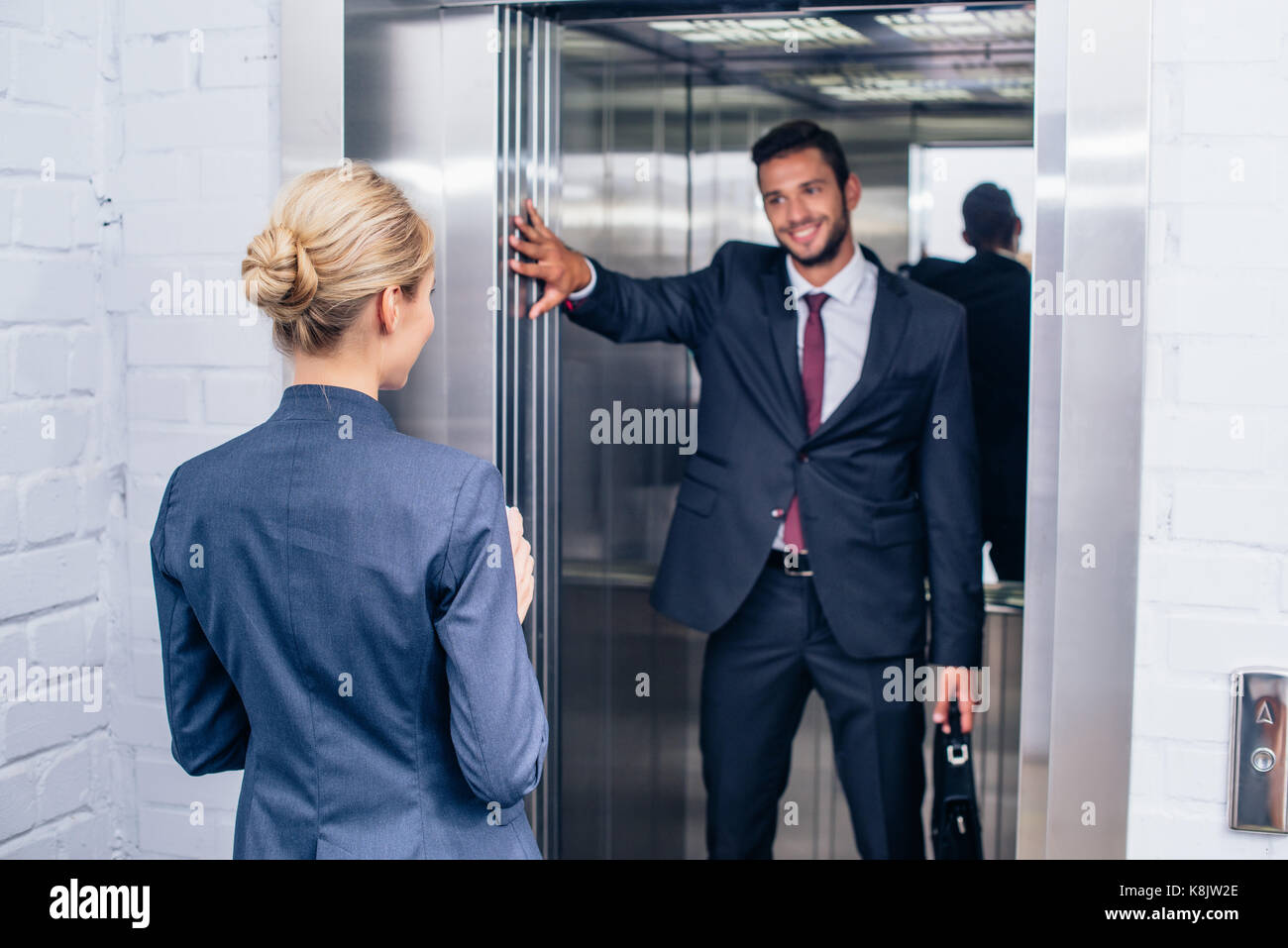businessman holding elevator door for woman Stock Photo - Alamy